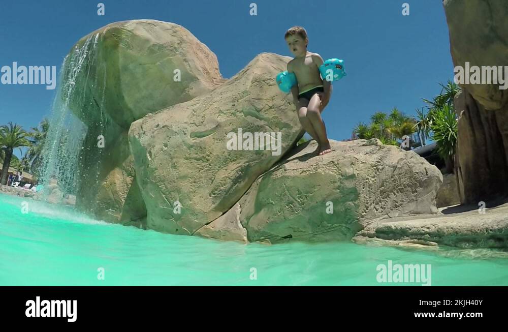 Boy is jumping from the cliff in the waterpark and diving in the pool ...