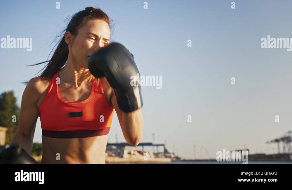 Young hardy woman in leather boxing gloves and sportswear is boxing ...