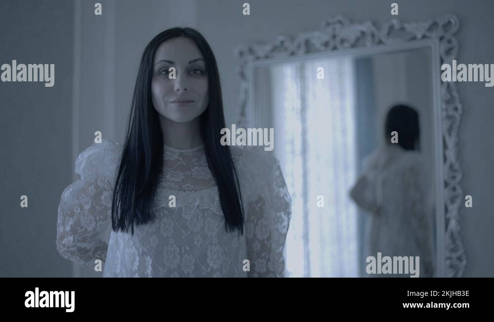 Scary woman in dress looking at camera, holding knife behind back ...