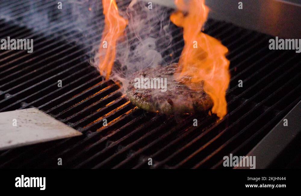 Chef cooking beef patty for burger on grill and flip the cutlet with ...