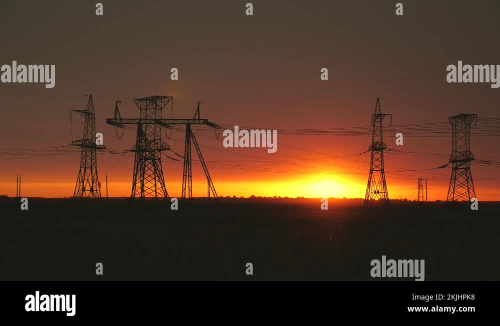 High voltage electrical lines in a field at sunset. The dark silhouette ...