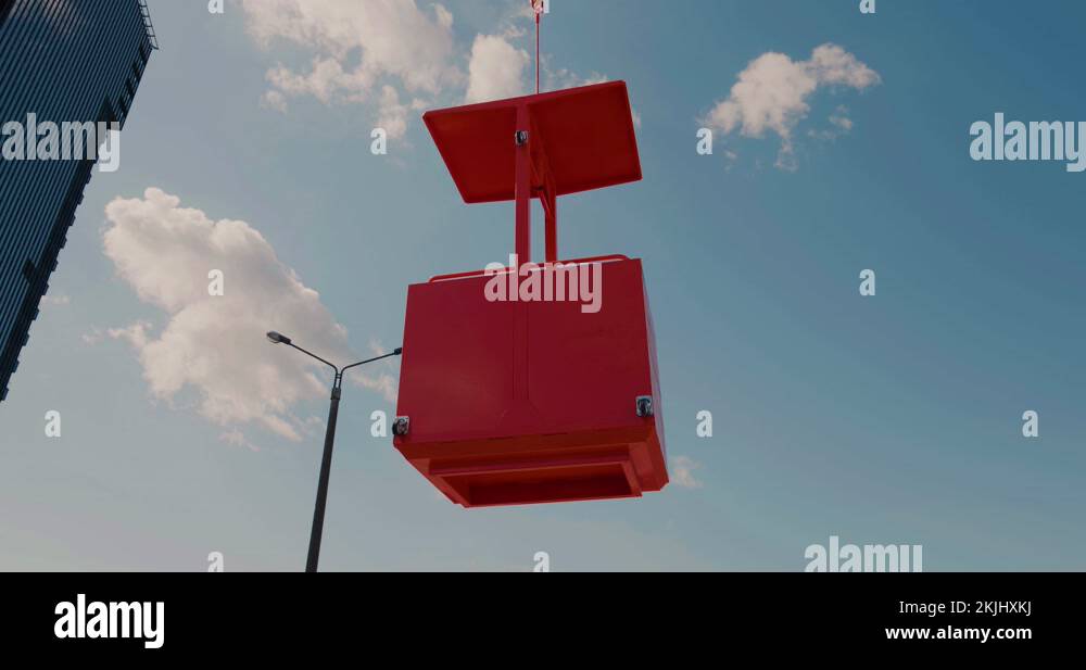 Close-up of an orange building cradle lifted by a crane lifts up to a ...