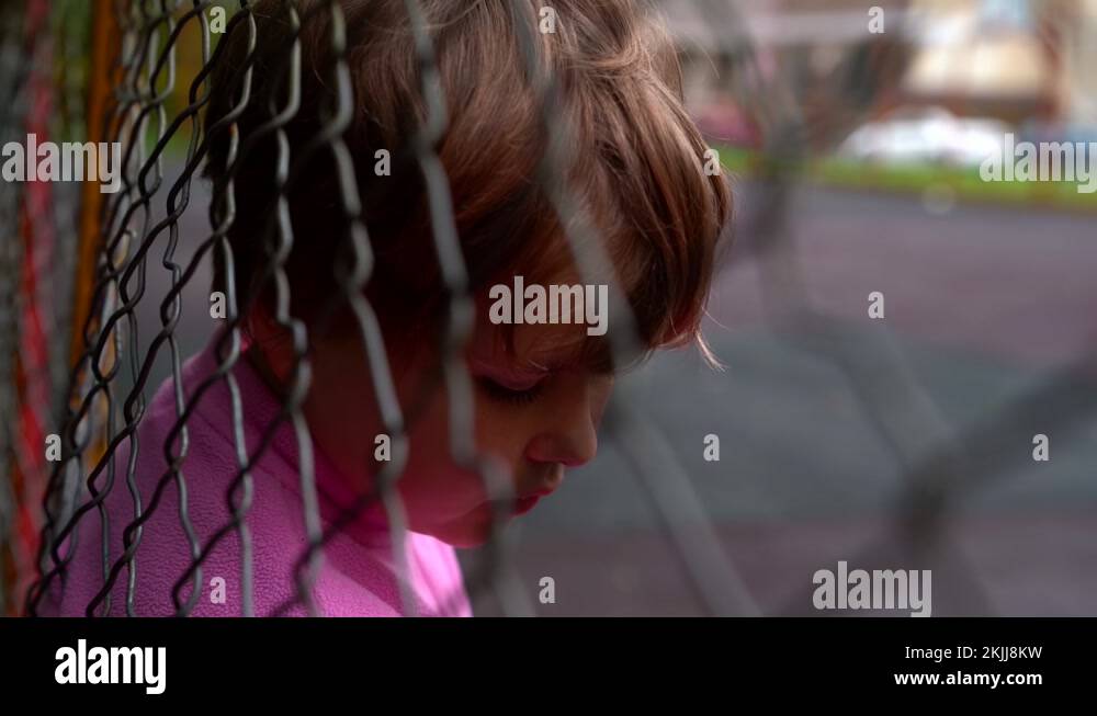 Close-up portrait of a child of a girl who stands behind a chain-link ...