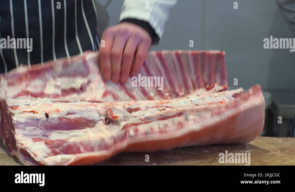 Butcher using knife and saw to cut portions of pork pig belly Stock ...