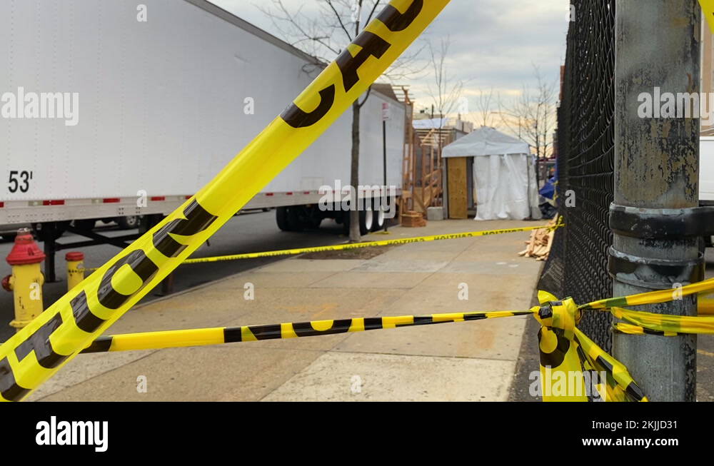 Healthcare workers behind yellow caution tape next to temporary morgue ...