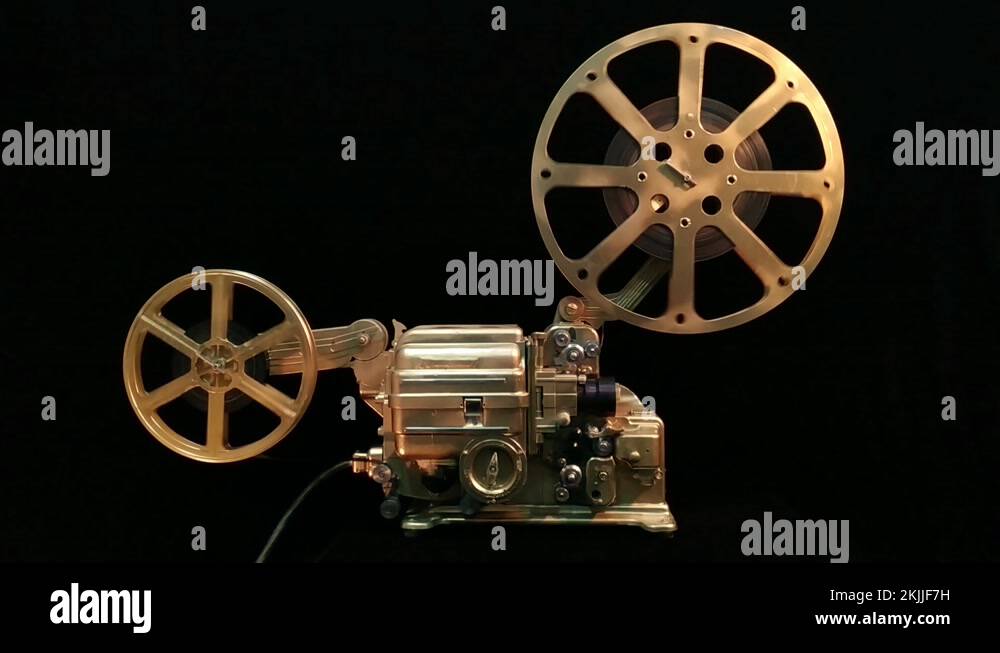 A working retro film projector of gold color in full face on a black ...
