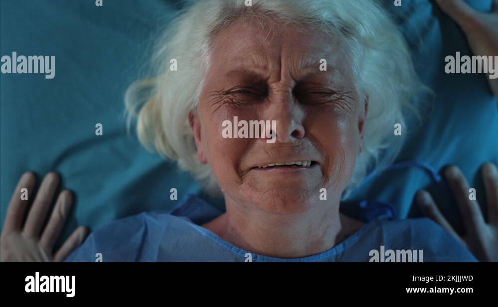 Old scared woman crying while lying on hospital stretcher. Top view of ...
