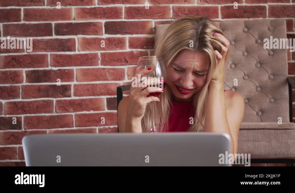 Upset crying blonde drinks red wine from a glass and looks at the ...