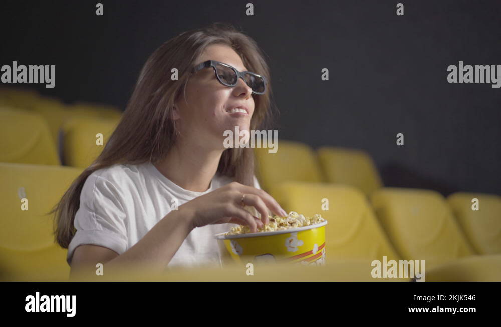 Single beautiful woman watching 3d film in cinema and eating popcorn ...