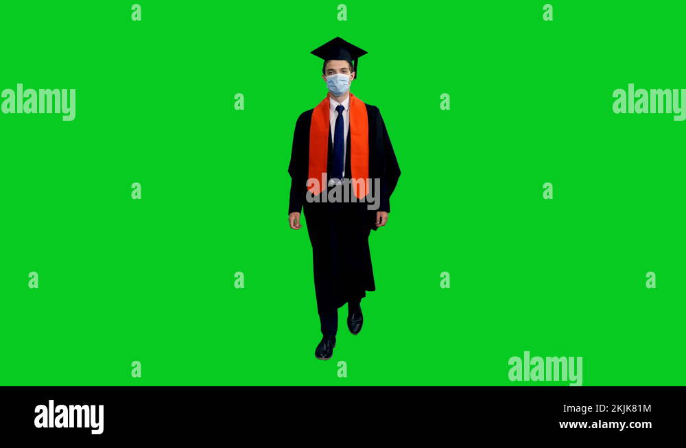 Graduating student in mask walking towards the camera on green screen ...