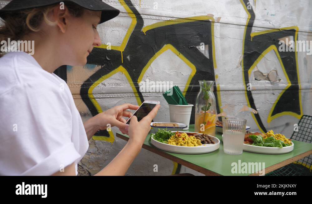 Girl in a bucket hat taking a picture of her breakfast sitting next to ...