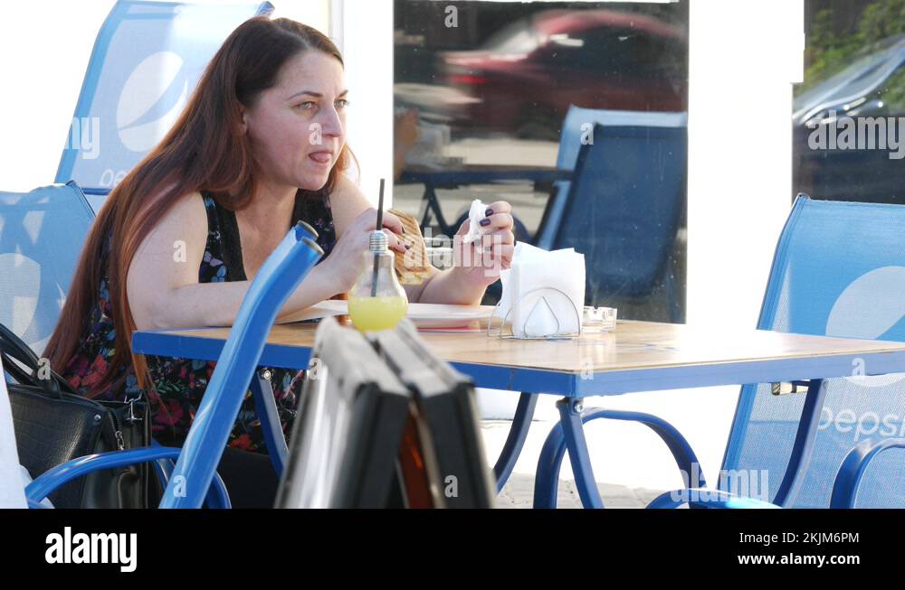 Young woman sits at a table of a summer cafe. Pretty lady is having a ...