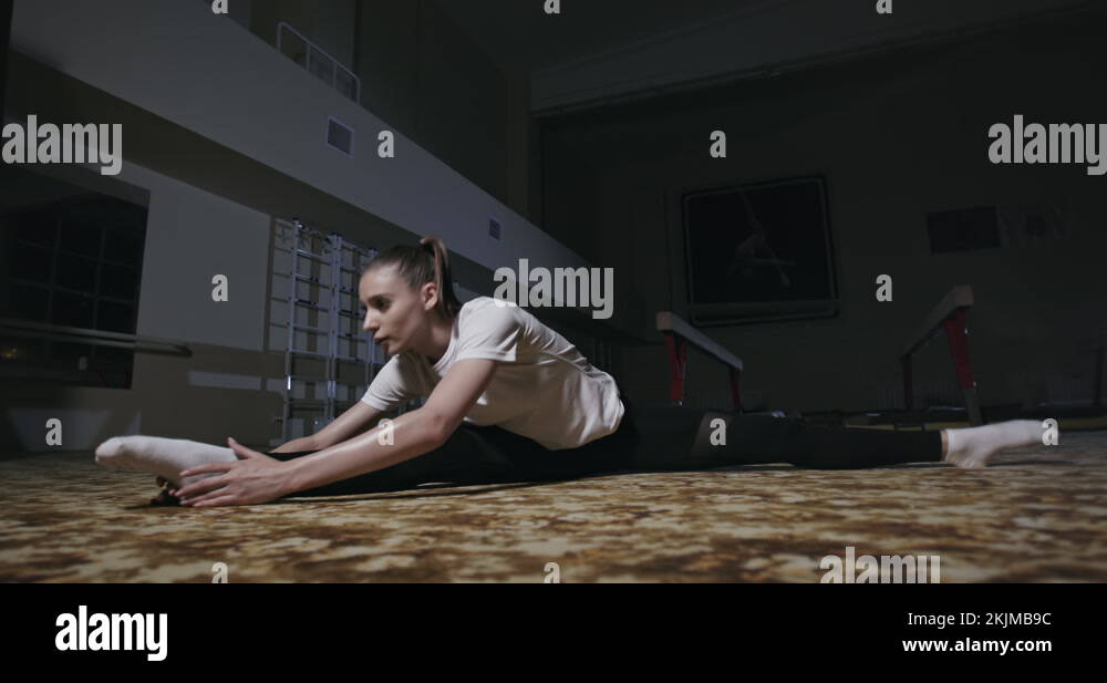 Young flexible sweaty female gymnast doing splits and bending while ...