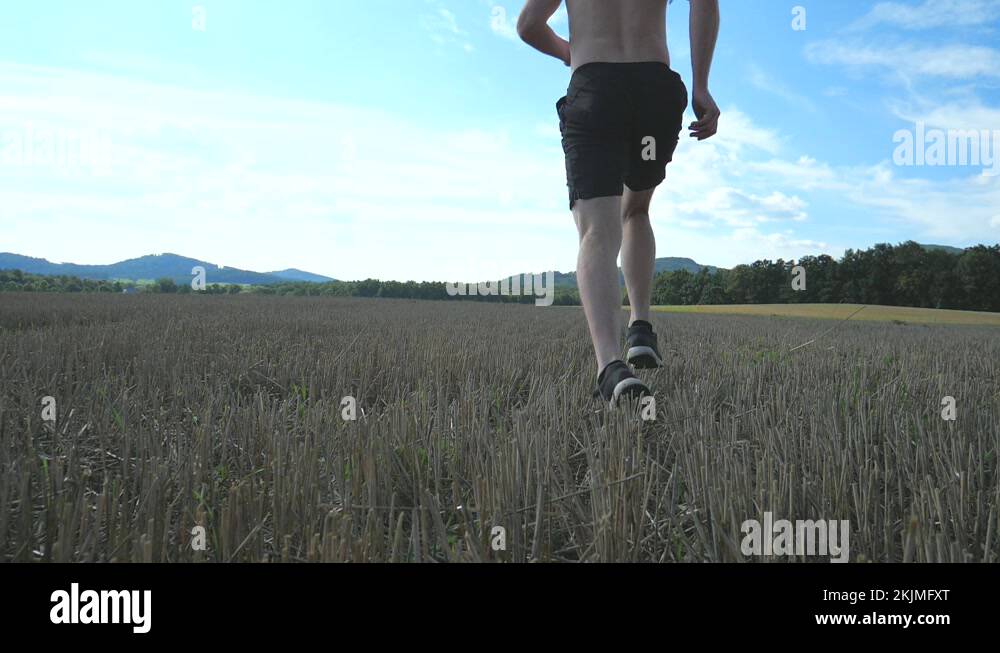 Shirtless sportsman running over harvested field. Legs of athlete with ...