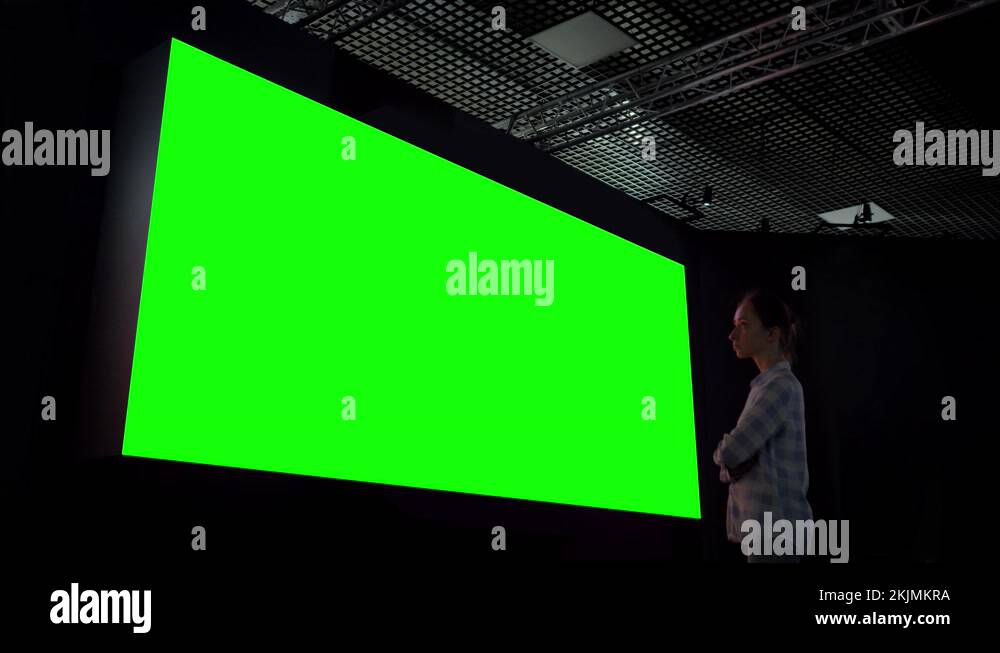 Woman looking at large blank green screen in dark room - chroma key ...