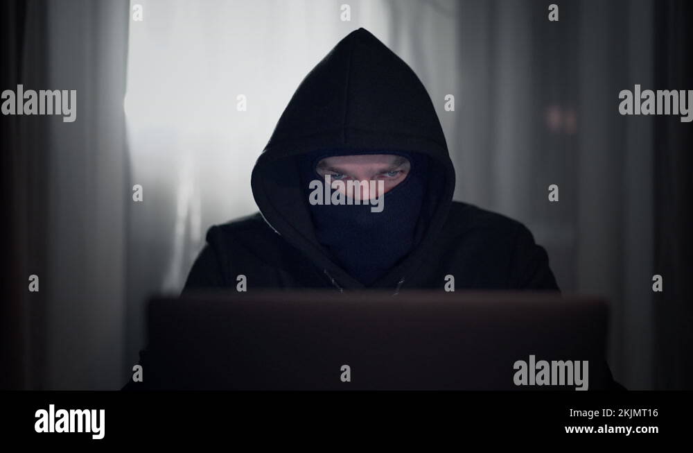 Hacker cracker in the hood in a dark room using computer virus program ...