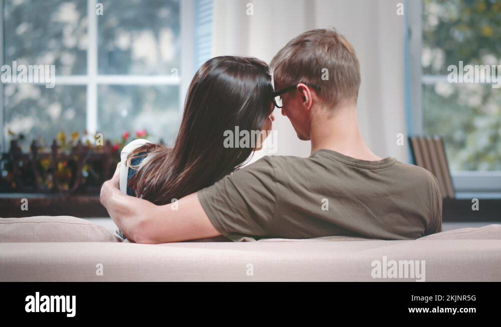 Back view of happy couple in love cuddling and kissing sitting on sofa ...