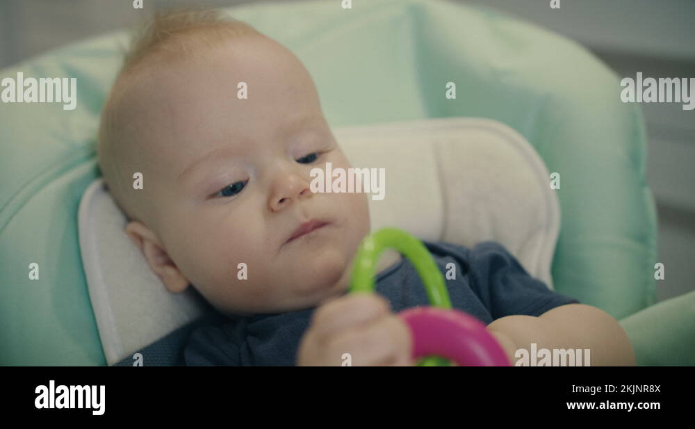Cute baby in kid chair plays with toy, bites it and smiles during ...