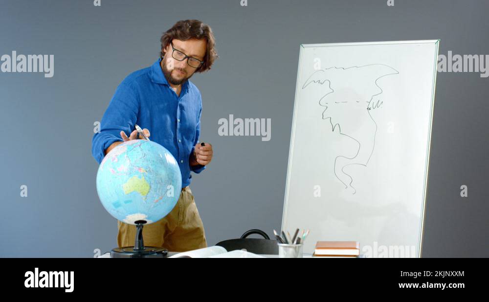 Caucasian male teacher in glasses standing at board and drawing map in ...