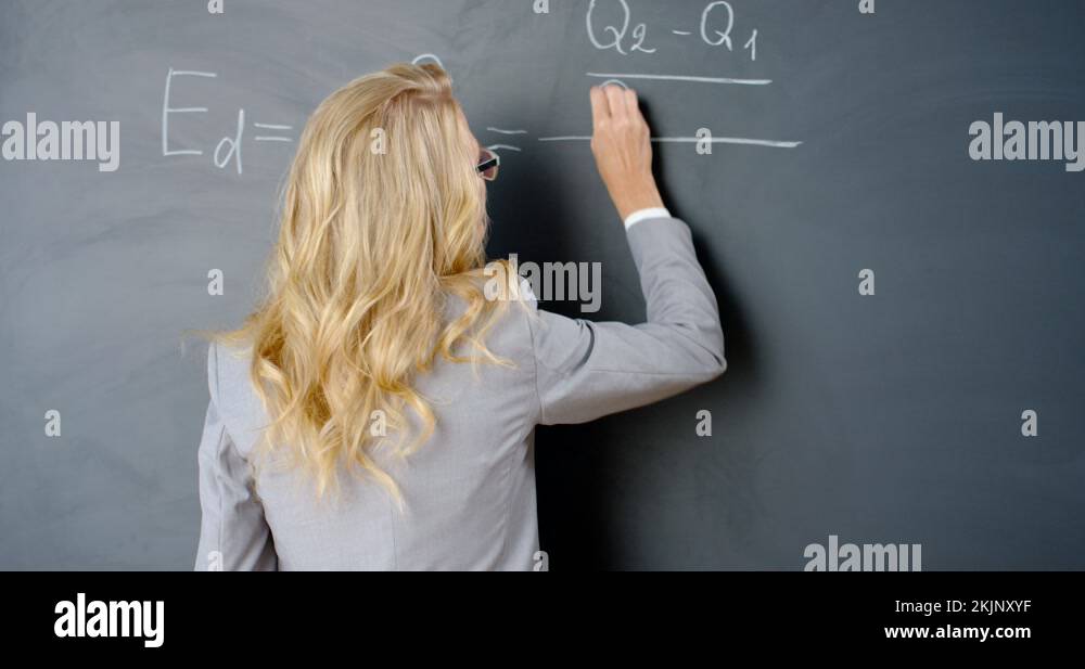 Back view on Caucasian female lecturer writing math or physics formulas ...