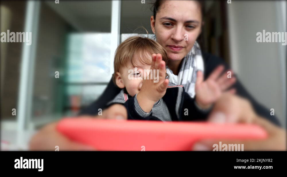 Toddler boy clapping hands while on mom lap watching smartphone screen ...