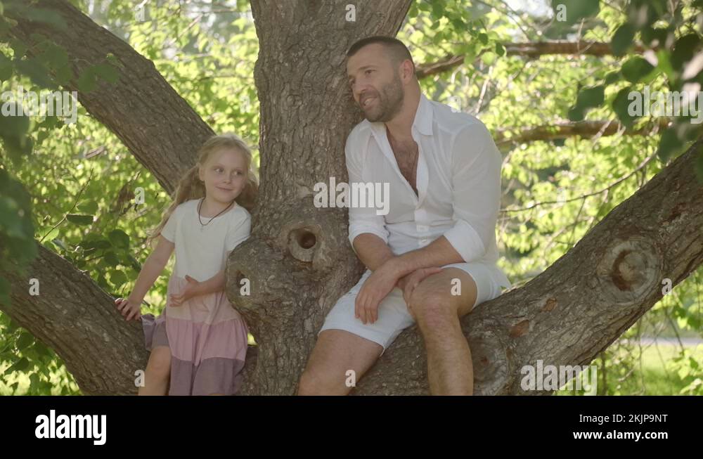 dad and daughter are sitting and playing in the tree. a young father ...