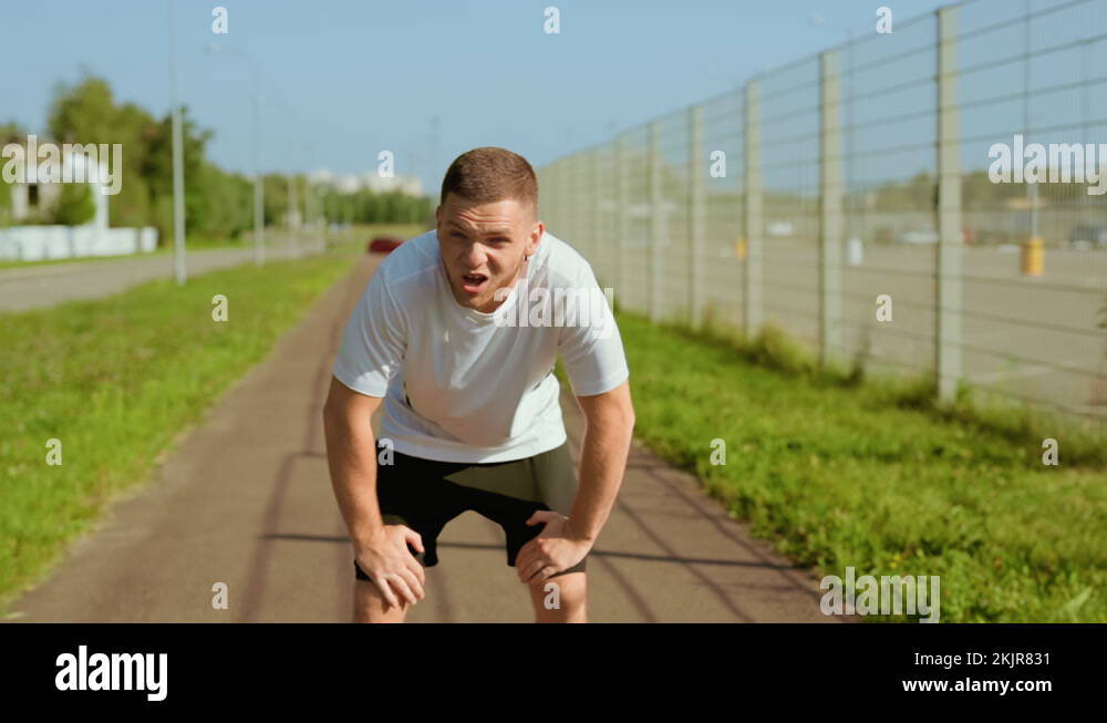 Tired sporty man stop after run look at camera nervous on urban street ...
