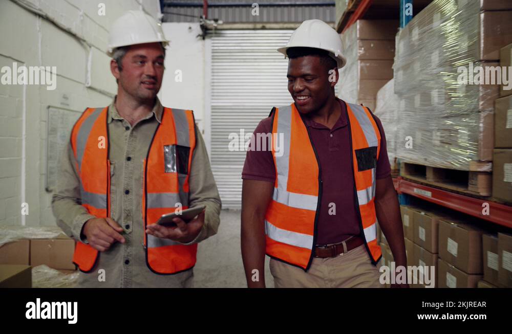 Two friendly colleagues walking down aisle in factory shop checking ...