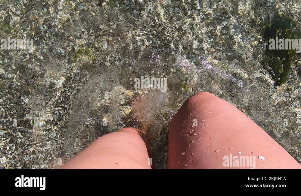 Girl standing knee-deep in water on beach with brown sand and shells ...