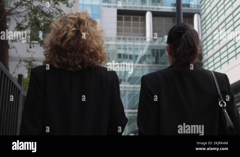 Back view of women in formal clothes walking towards office buildings ...