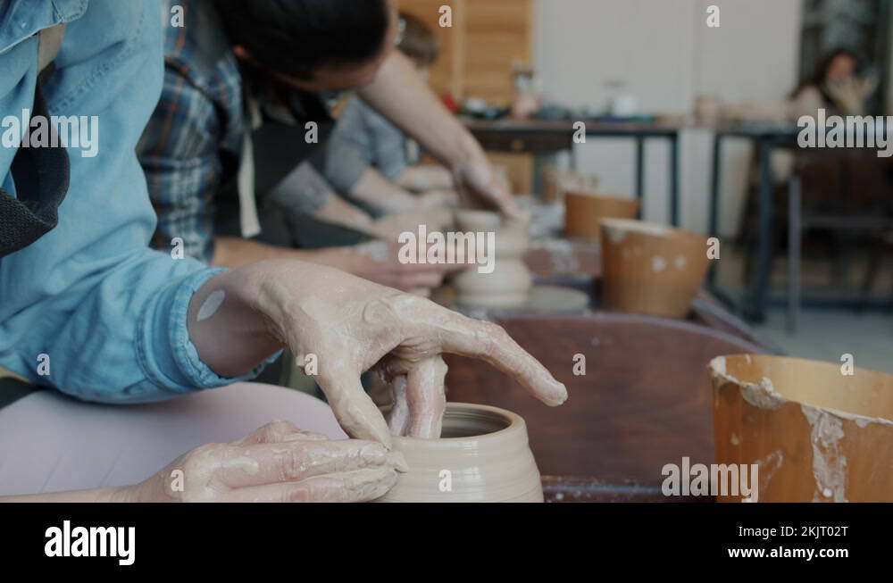Close-up tilt-up of young woman making pot on throwing-wheel in pottery ...