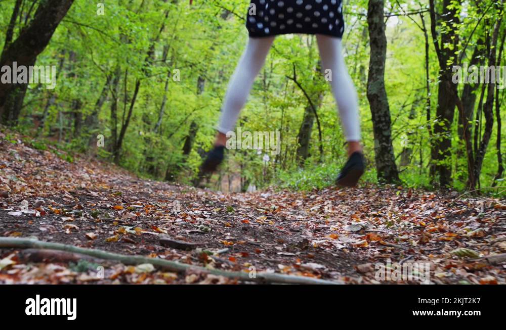 The legs of a little girl run and jump happily along the forest path ...