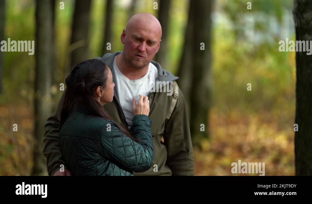 Happy adult married couple hugging and talking in the woods. A bald ...
