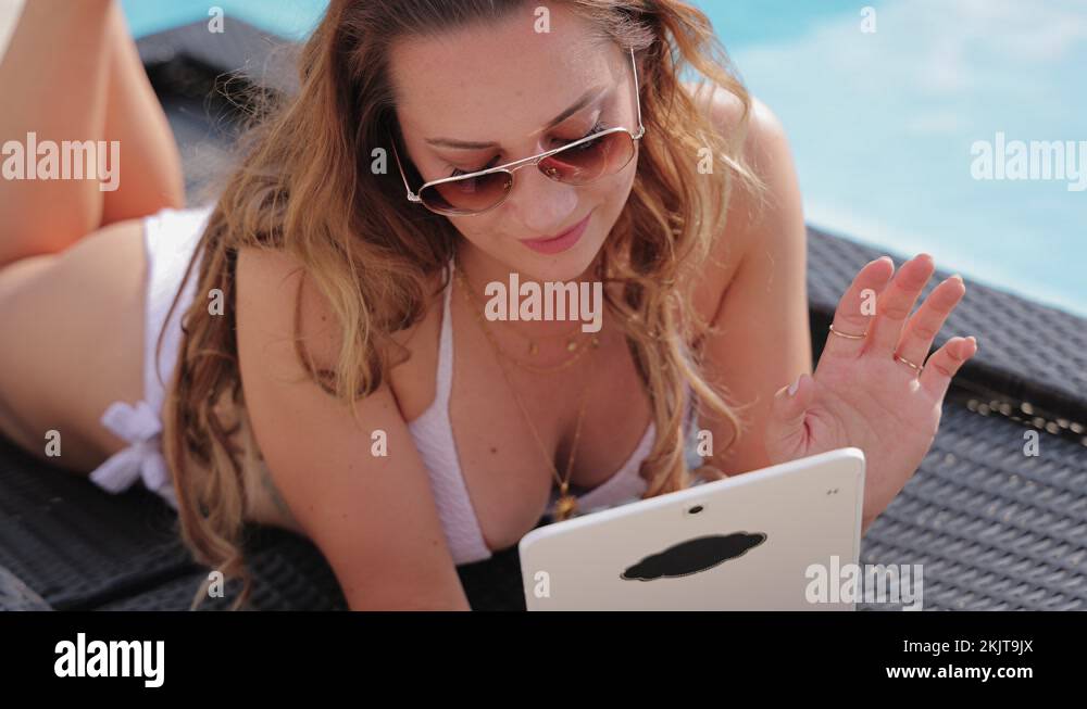 Young woman in bikini relaxes with a tablet by the swimming pool Stock Video Footage - Alamy