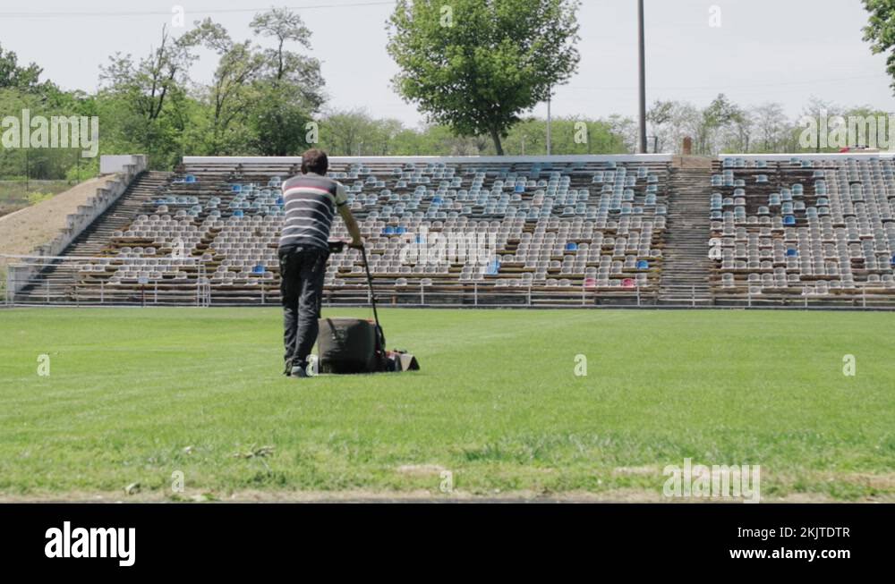Worker back to camera going and cutting grass using mower on the ...