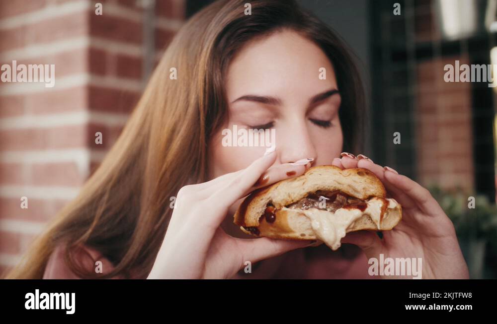Beautiful student girl eating burger in restaurant enjoying delicious ...