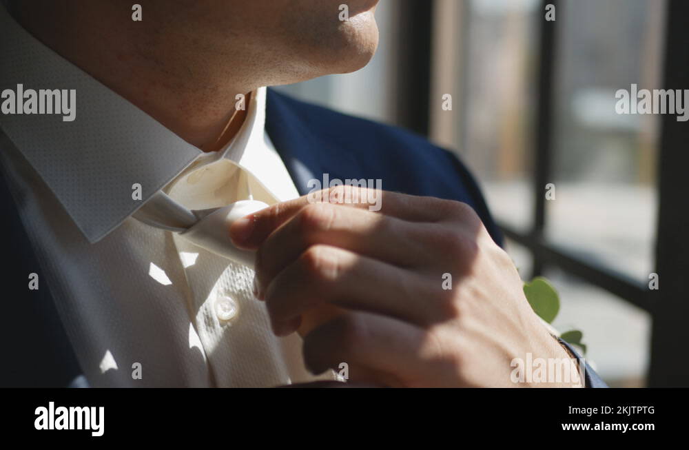 the groom's hand tying a tie by the window before the wedding ceremony ...