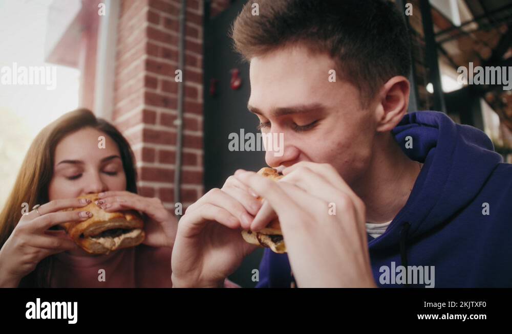 Young friends students eating unhealthy food or veggie burgers enjoying ...