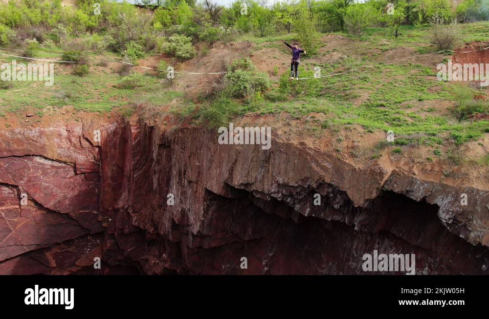 A man is turning around and balancing on the tightrope over a huge pit ...