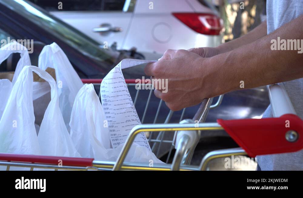 Worried man checks a paper receipt after grocery shopping at a ...