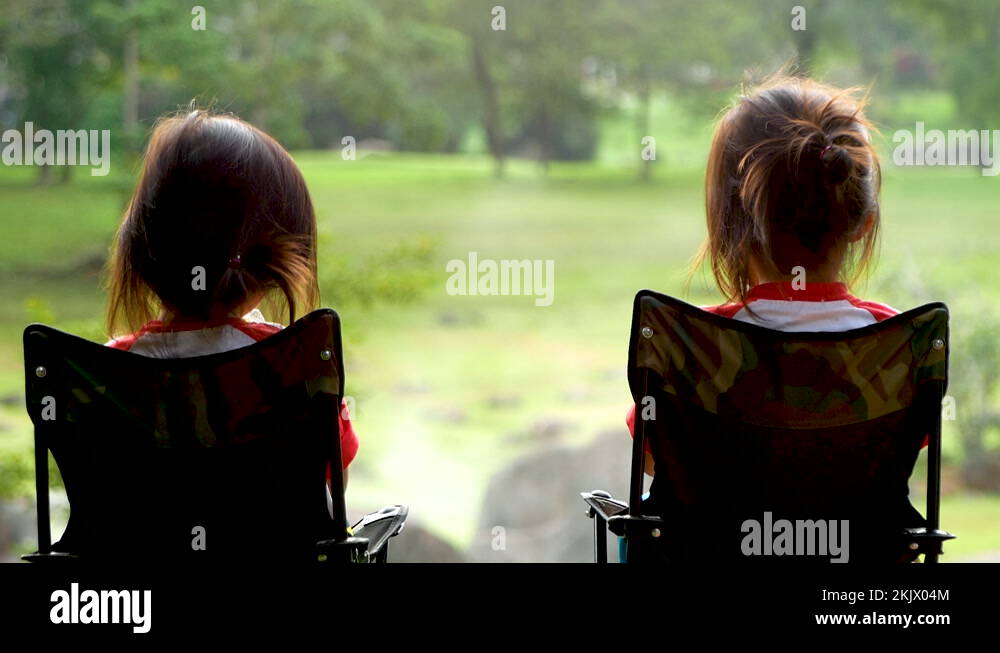 Back view of two girls sitting on deck chairs enjoying breakfast at ...