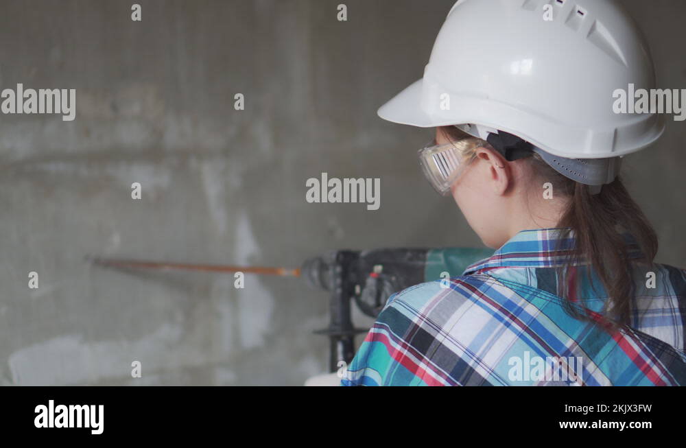 Young Female construction worker drilling concrete wall with the drill ...