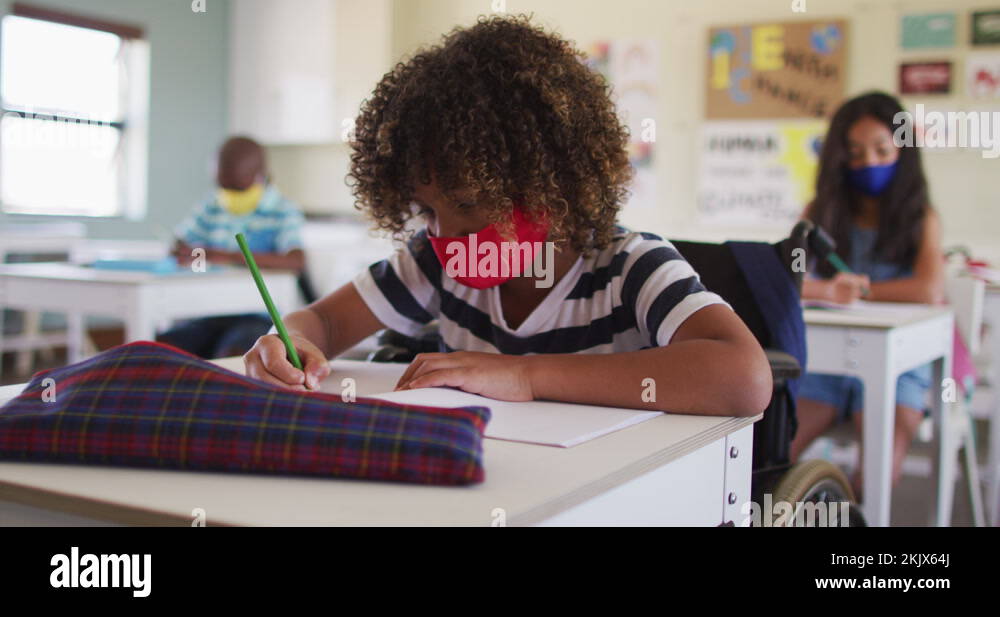 Disable boy wearing face mask writing while sitting on his wheelchair ...