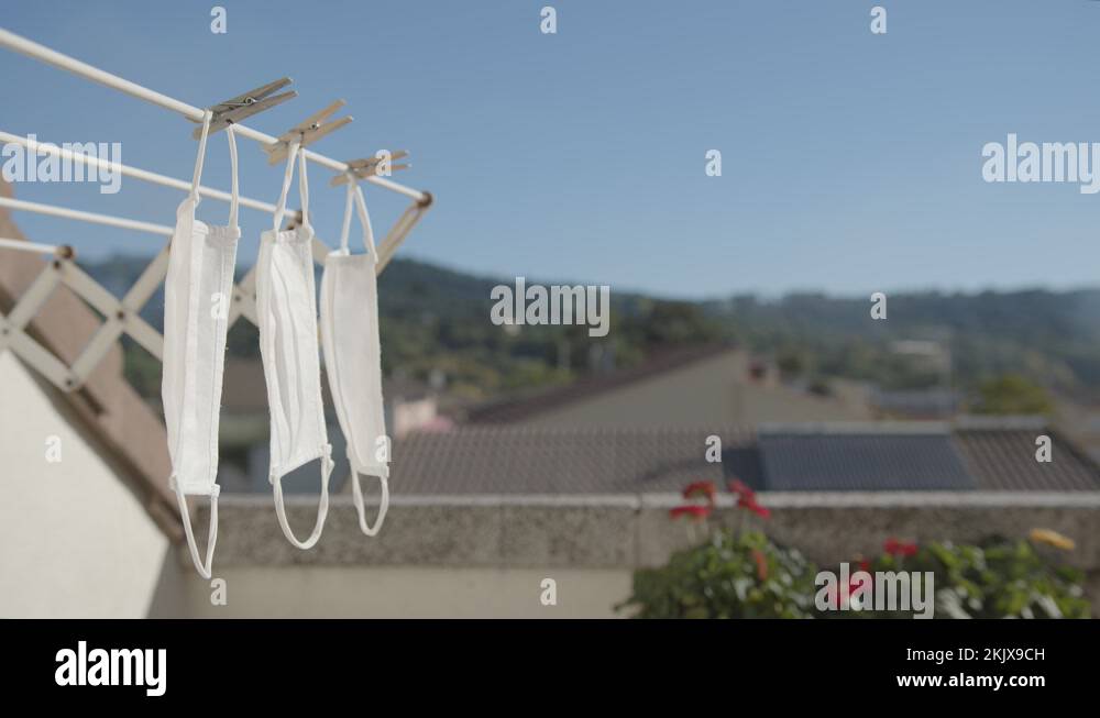 Three white masks hang in a clothesline with a soft wind in the terrace ...