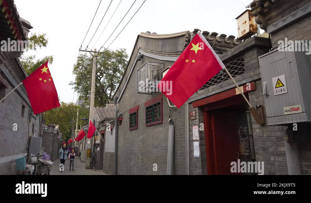 People walking in Hutong lane with Chinese flags hung on rhe wall ...