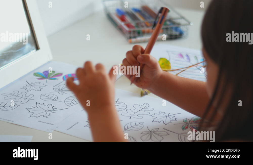 Little girl coloring different types of leaves on a paper sheet with a ...