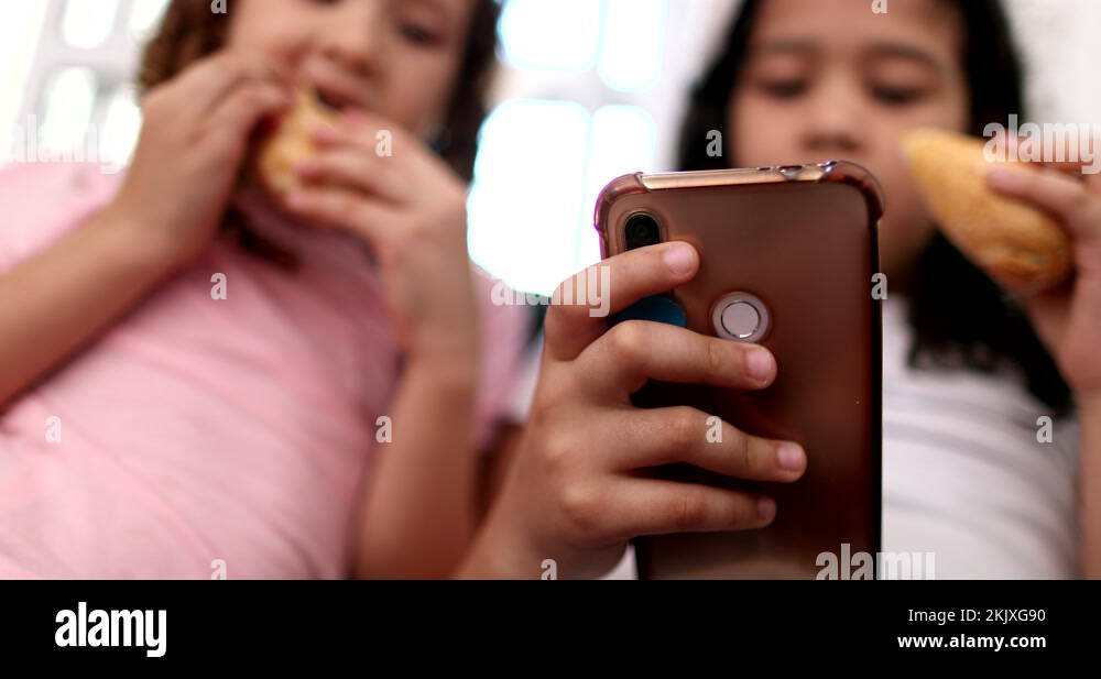 Generation Z little girls using mobile phone while eating sandwich ...