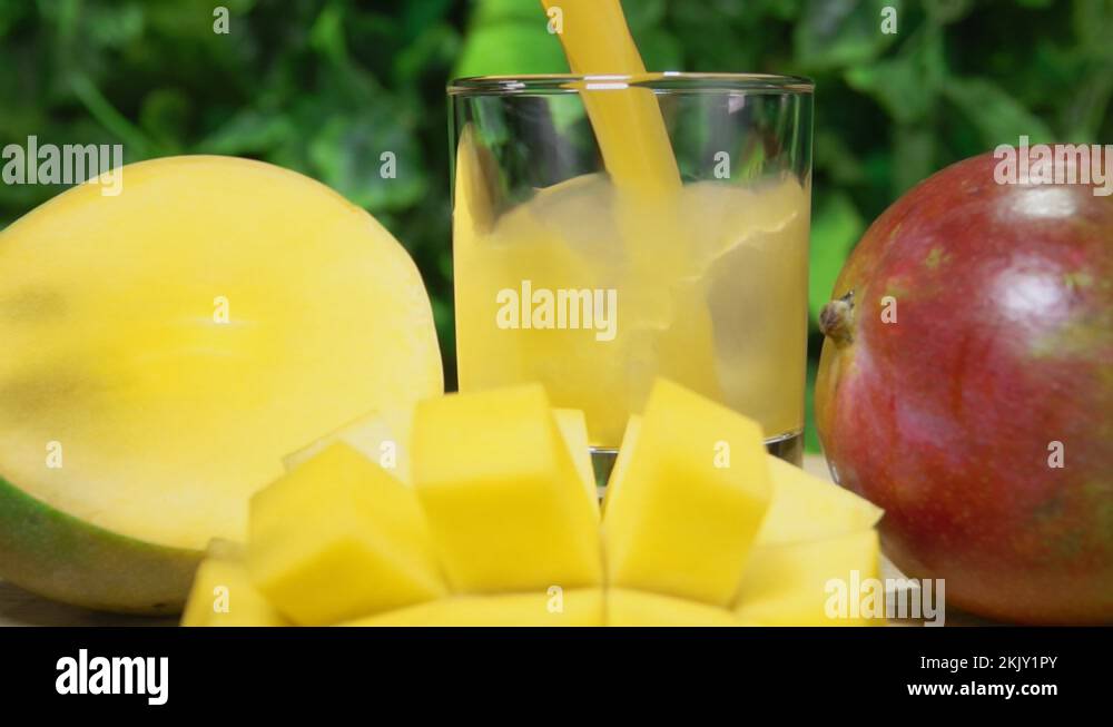 Mango juice is poured into the glass next to large ripe mango cut into ...