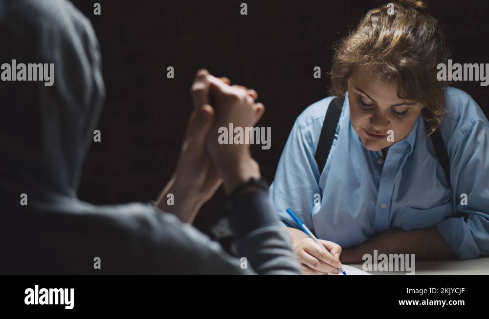 Female police officer interrogating criminal in handcuffs at desk in ...