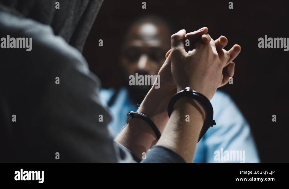 Police officer interrogating criminal in handcuffs at desk indoors ...
